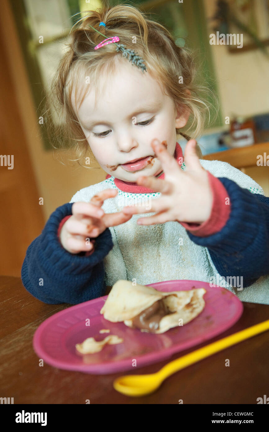 Toddler playing with hands while eating snack Stock Photo - Alamy