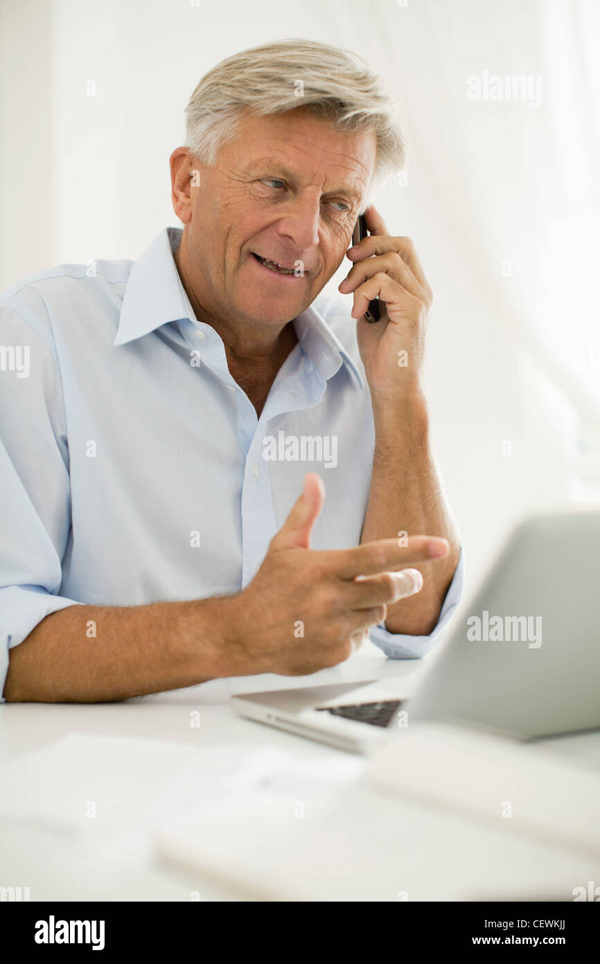 Man talking on cell phone while using laptop computer Stock Photo - Alamy