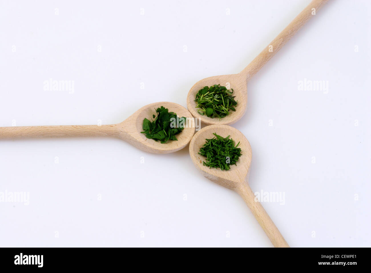 A close up of three wooden spoons with chopped thyme, dill and parsley ...