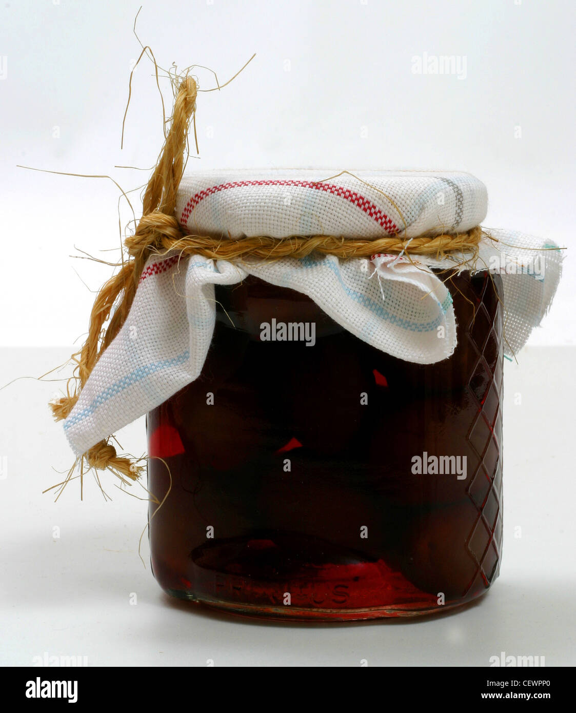 A jar filled with red liquid with a cloth cover held in place with ...
