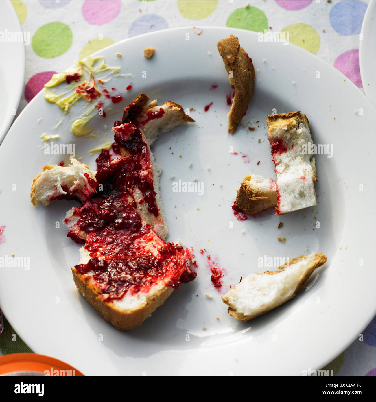 White china plate, half eaten pieces of white bread with butter and jam ...