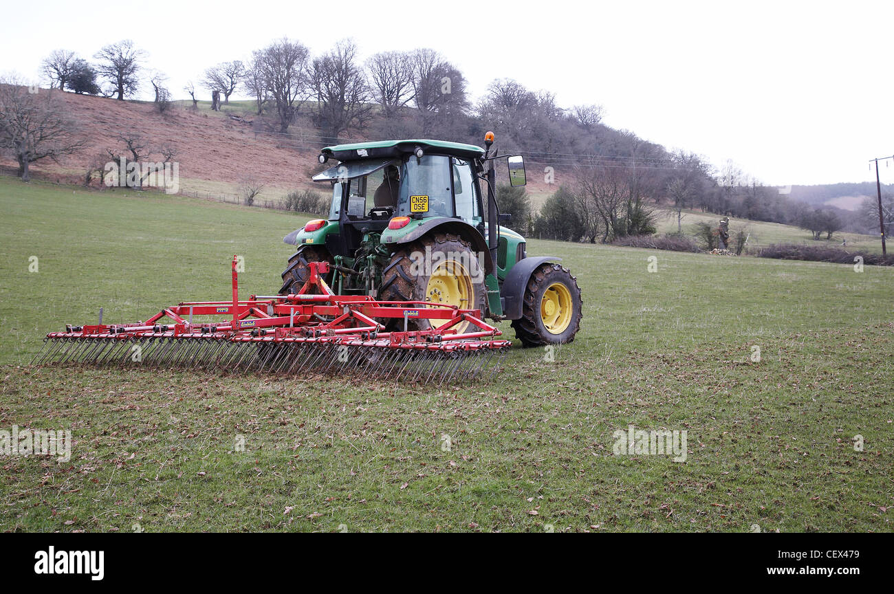 Farmer in tractor, aerating a field with grass harrows attachment on a ...