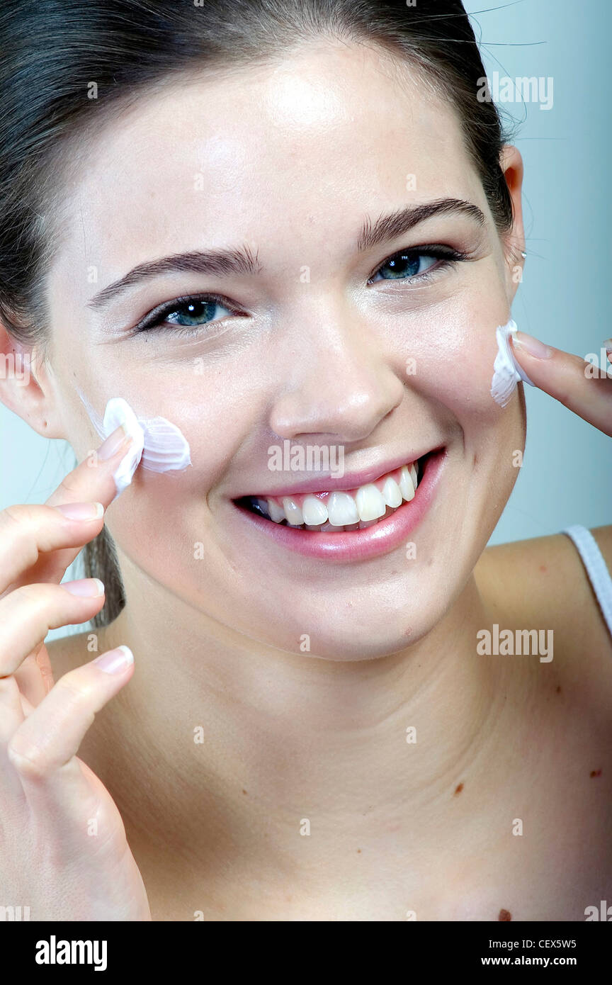 Female with brunette hair worn up, pale pink lips, rubbing a dab of ...