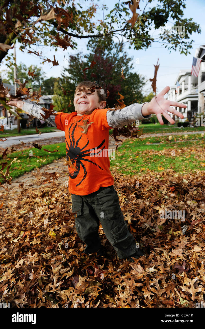 A laughing, playing 4-year-old caucasian boy in fall leaves with long ...