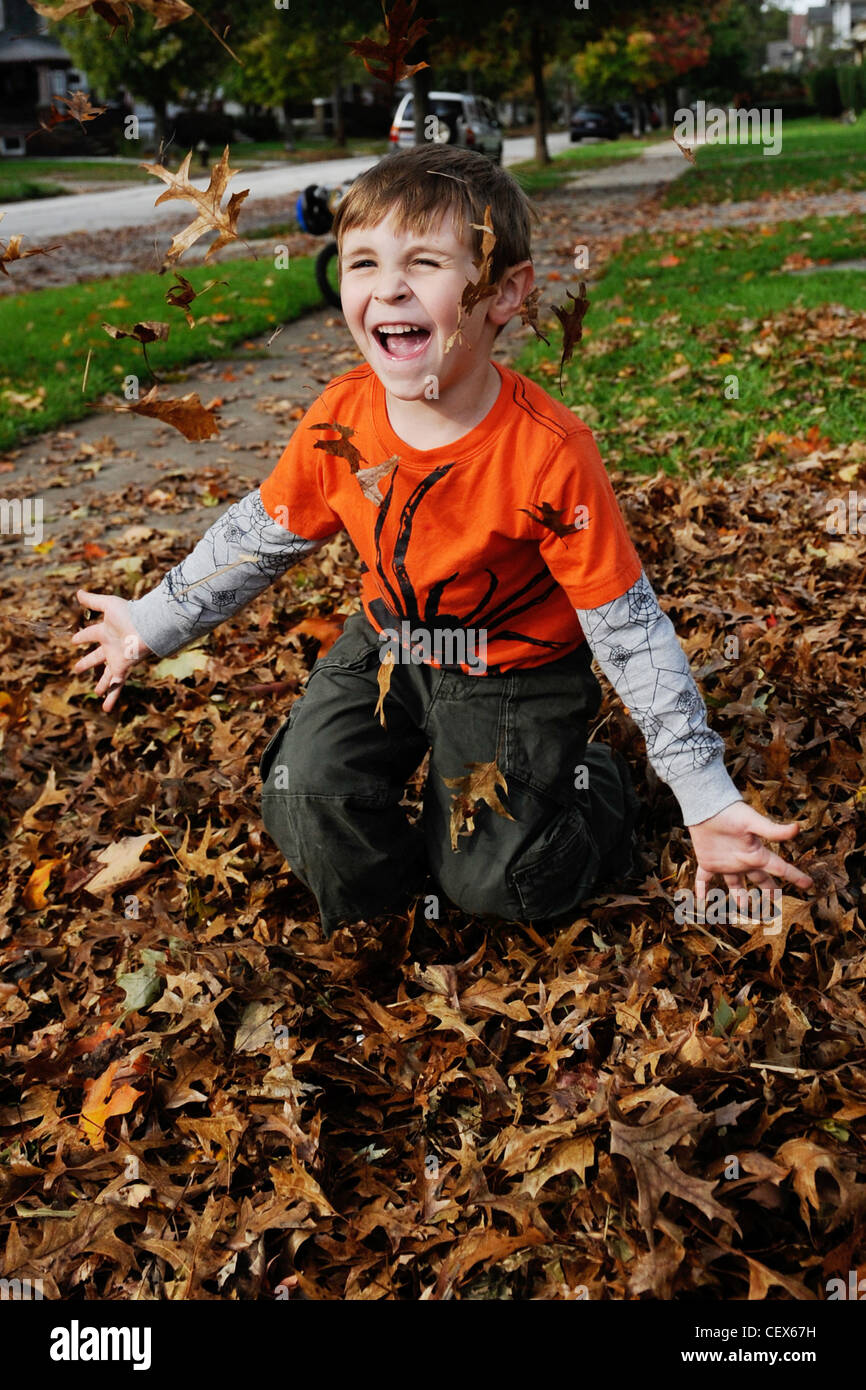 A laughing, playing 4-year-old caucasian boy in fall leaves with long ...