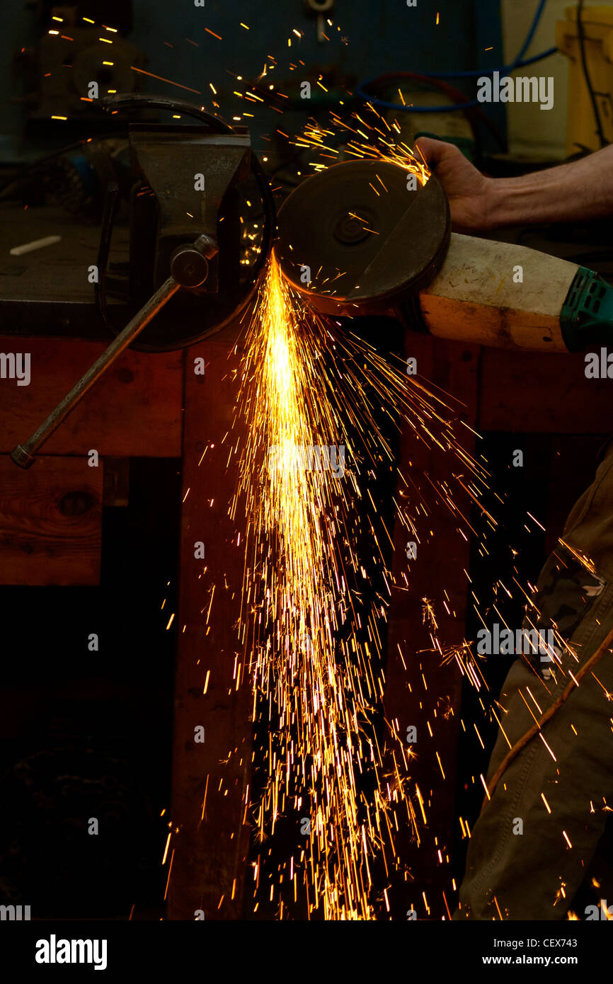 Working blacksmith refining a piece of metal by grinding to smooth the ...