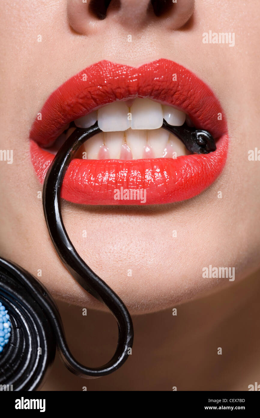Female wearing bright red lipstick biting a strand of liquorice Stock ...