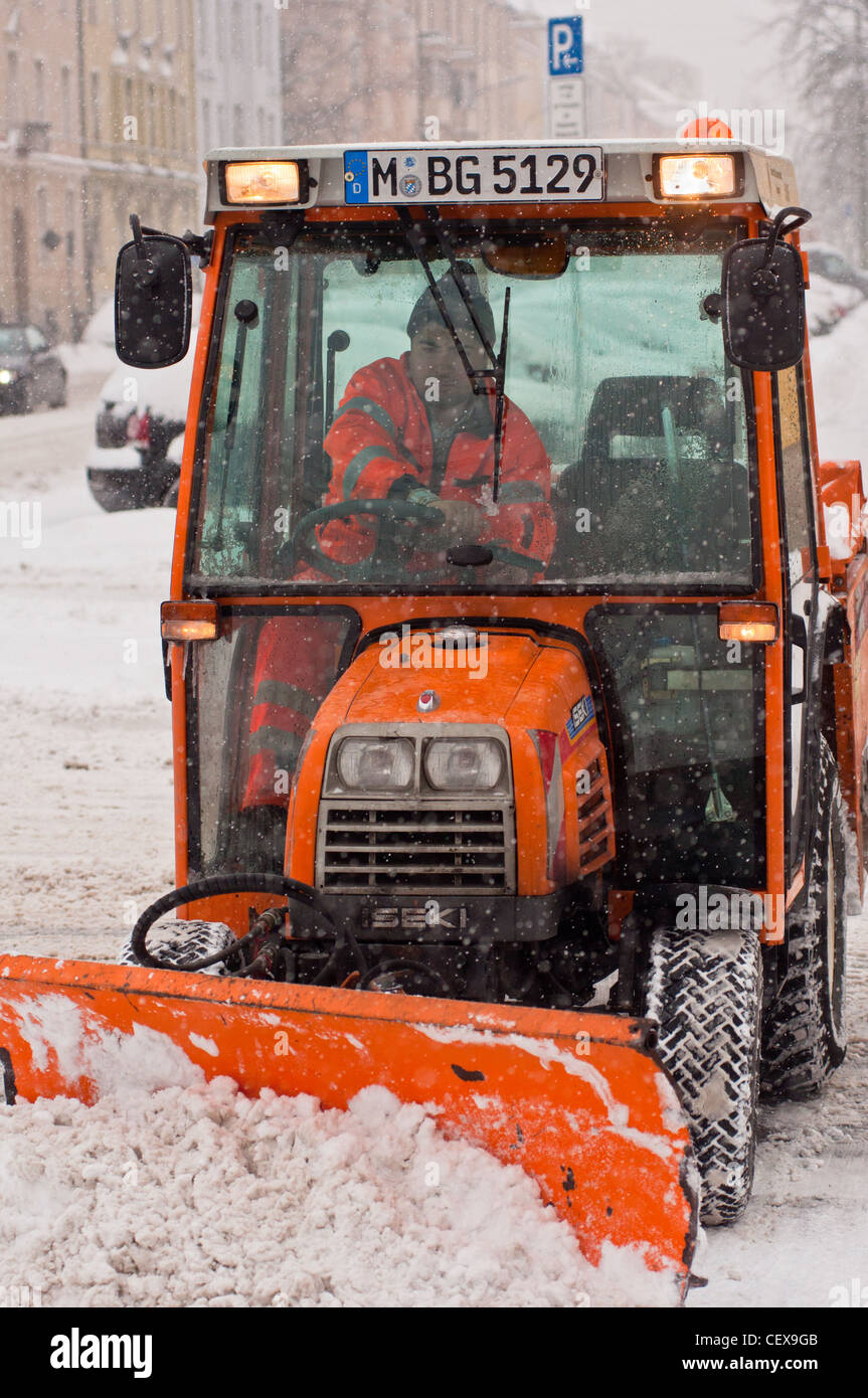 A snow plow with driver hard at work clearing the streets of Munich ...