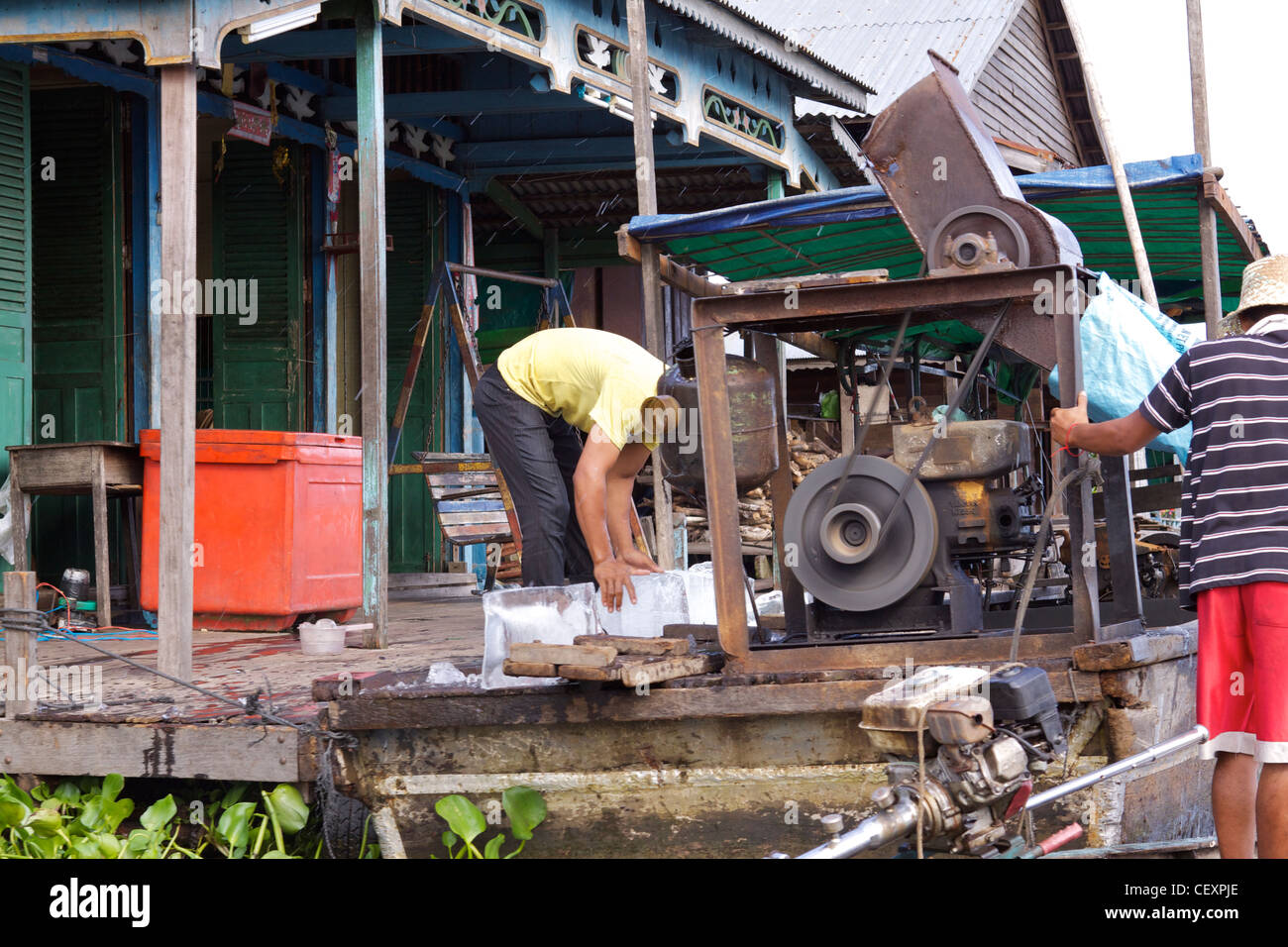 Two men work at a floating ice factory making and crushing ice for use ...