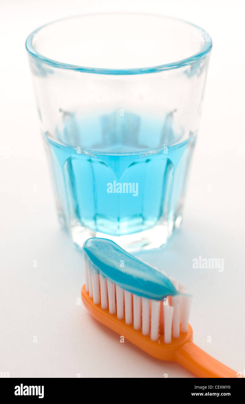 White and blue striped toothpaste on an orange toothbrush, with a glass ...