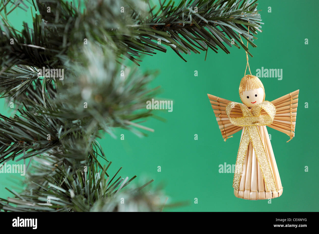 A straw angel shaped tree decorations hanging off the branch of a ...