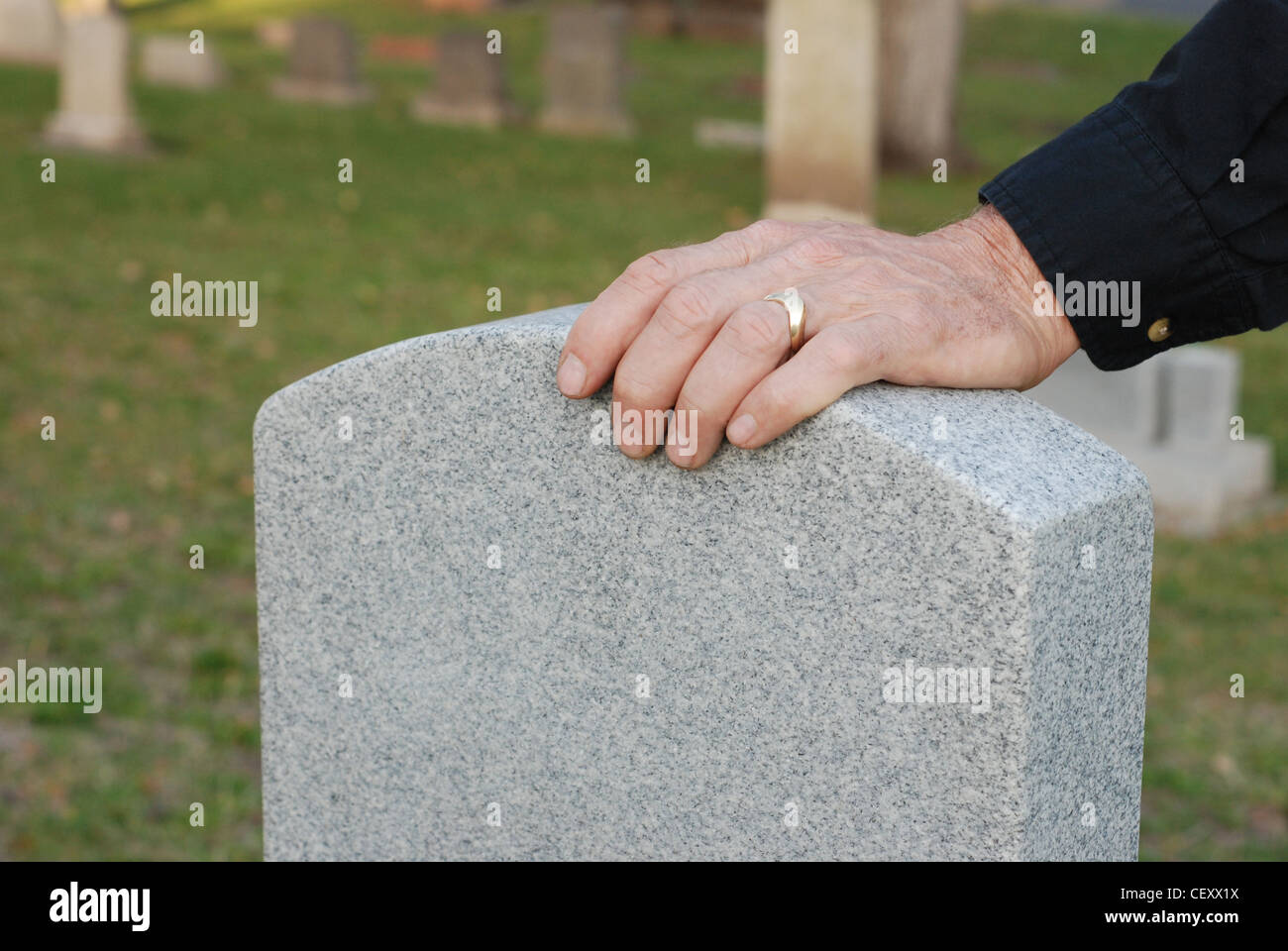 Close up of a man's hand, with wedding ring, resting on a headstone in ...