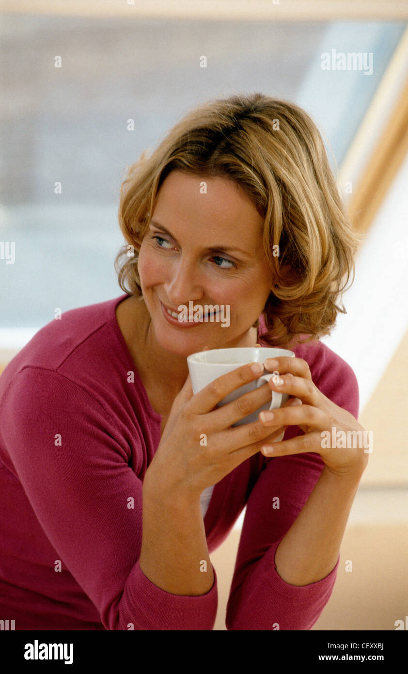 Female with short fair hair, wearing a pink cardigan, holding a white ...