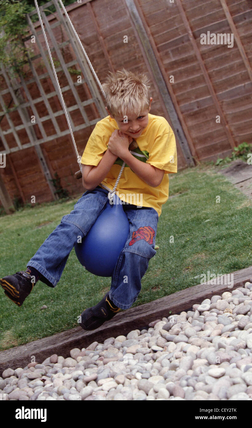 Male child spiky blonde hair hanging off blue rubber ball swing leaning ...