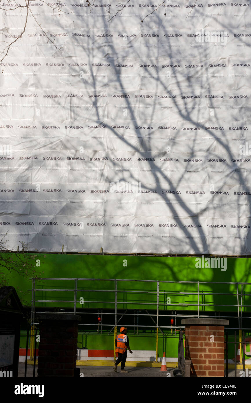 Construction workman below safety sheeting with plain tree shadow at a ...