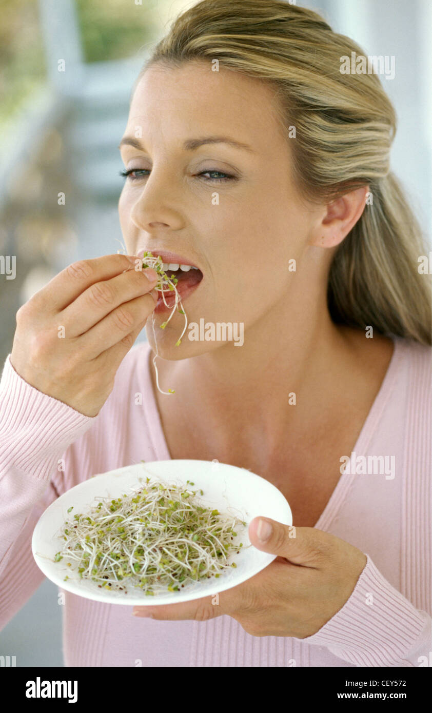 Female with long blonde hair off face eating handful of cress from ...
