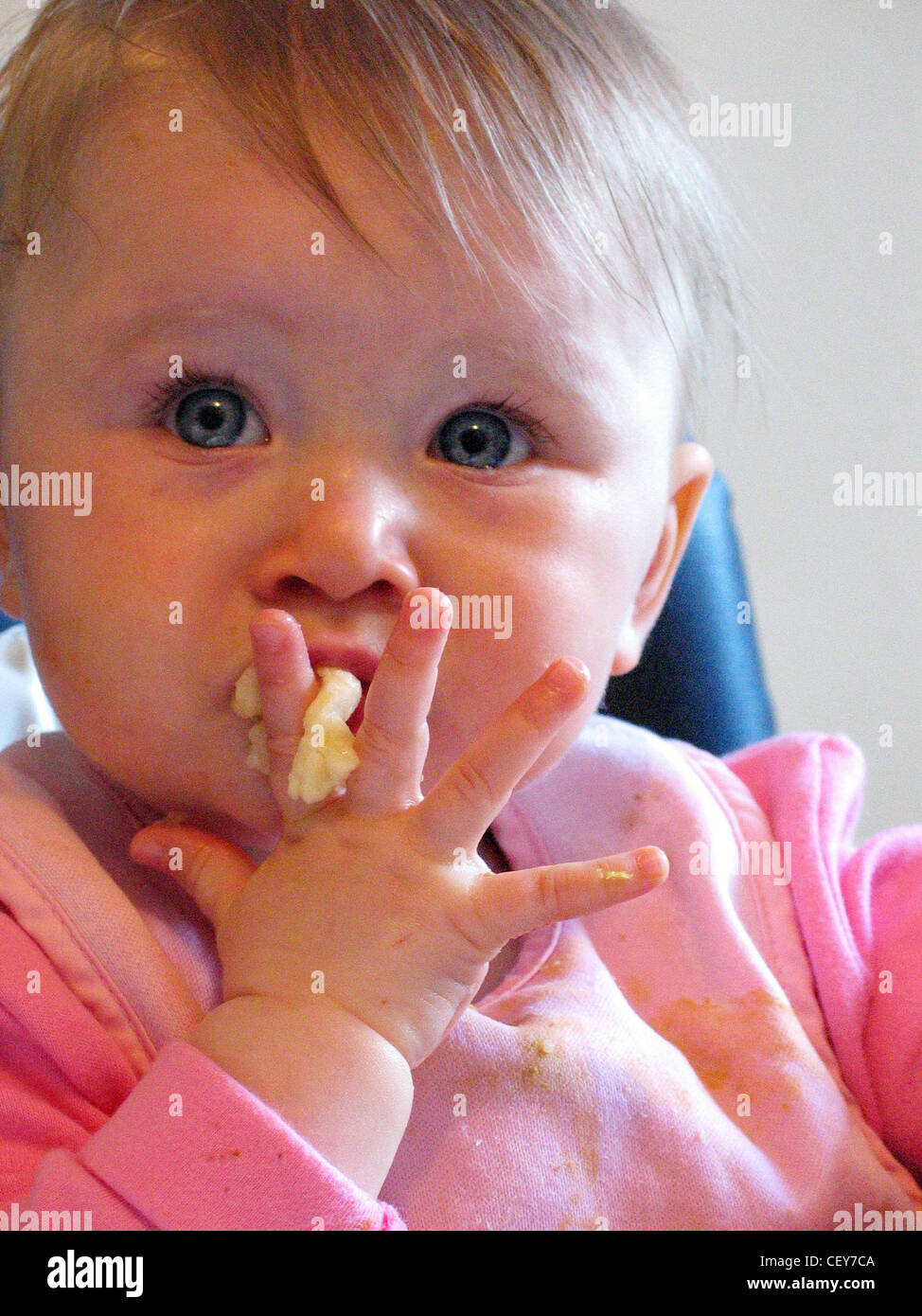 Baby with hand over mouth eating food and wearing a dirty bib Stock ...