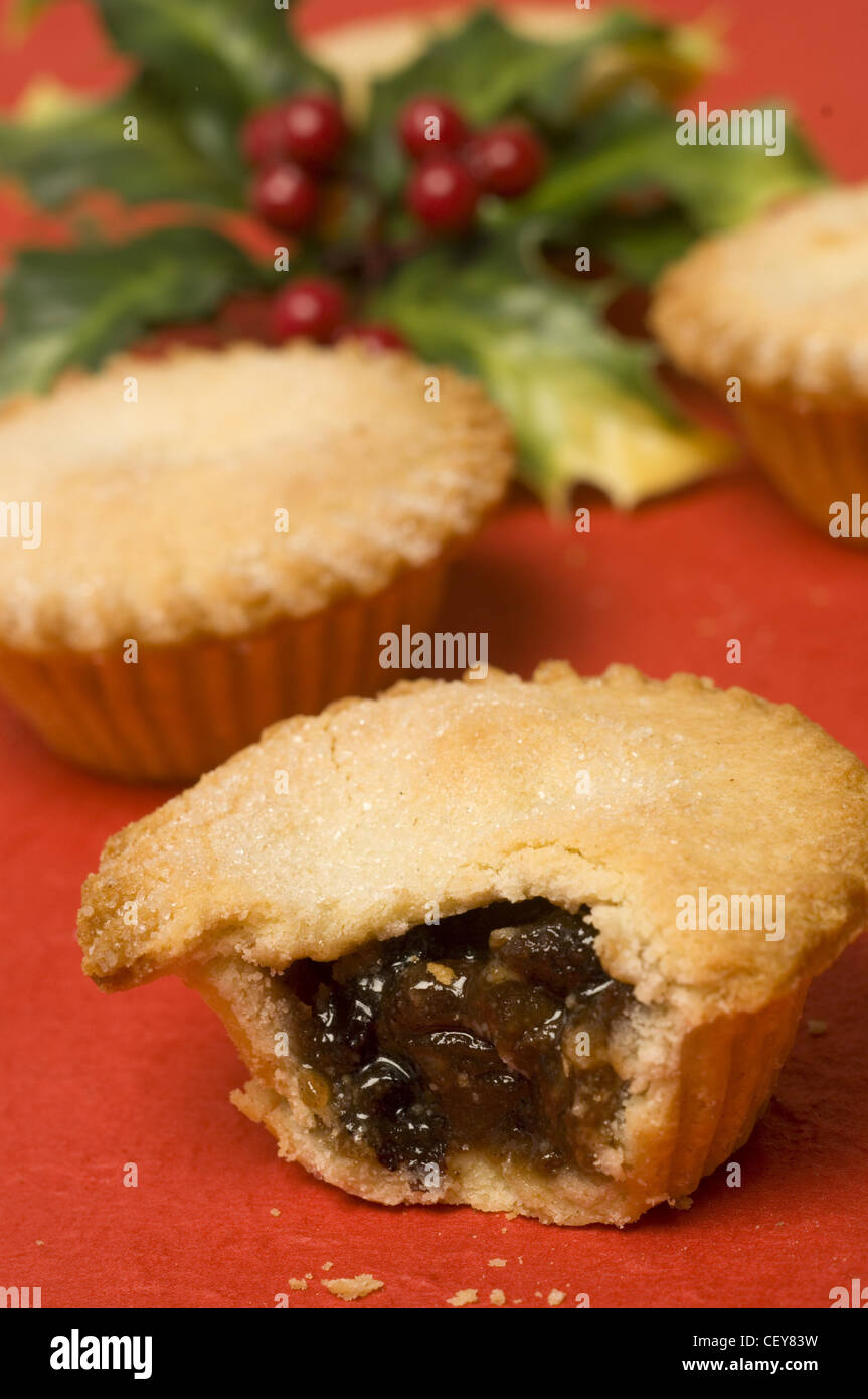 Three mince pies, half eaten pie in front , with cranberries in the ...