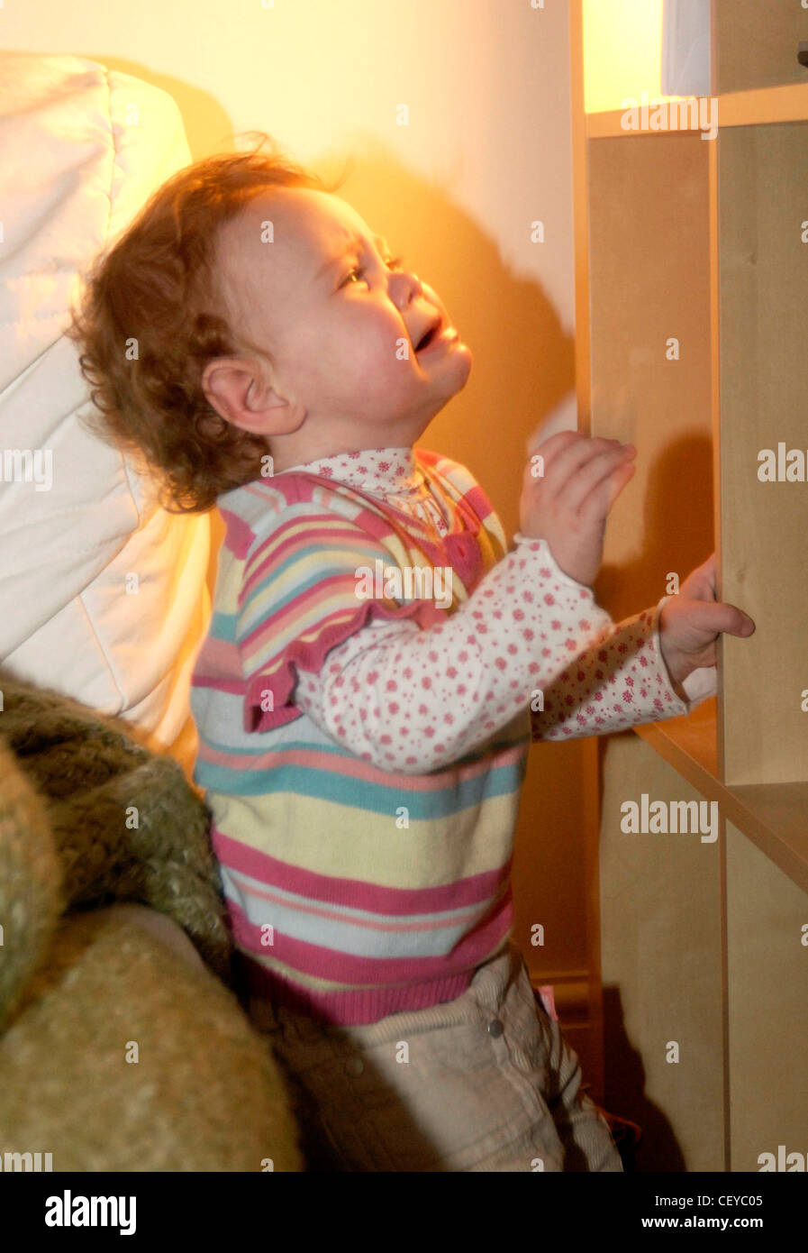 Toddler standing by light on bookshelf crying Stock Photo - Alamy
