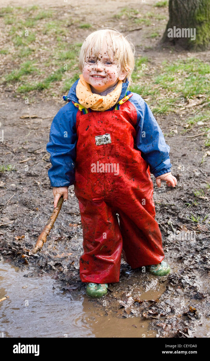 A male child standing by a large muddy puddle with mud splattered over ...