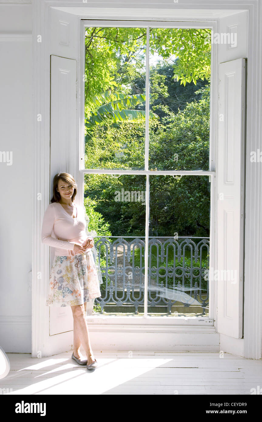 Female leaning against a white wall next to a large window wearing a ...