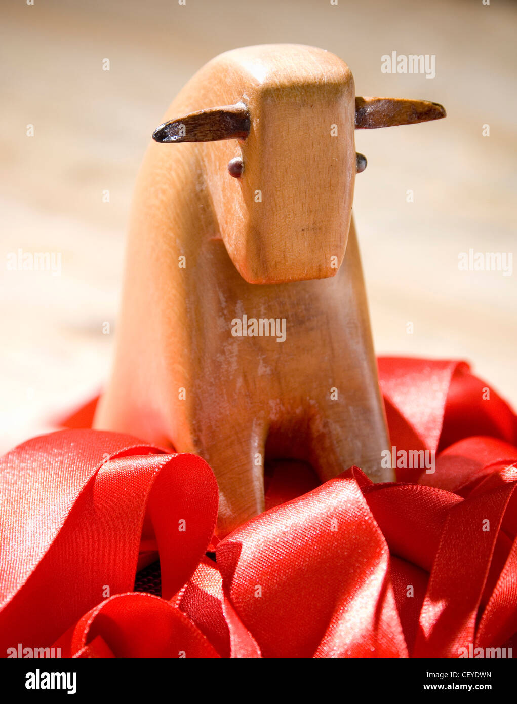 A still life of a wooden toy bull, sitting on a bed of red satin ...