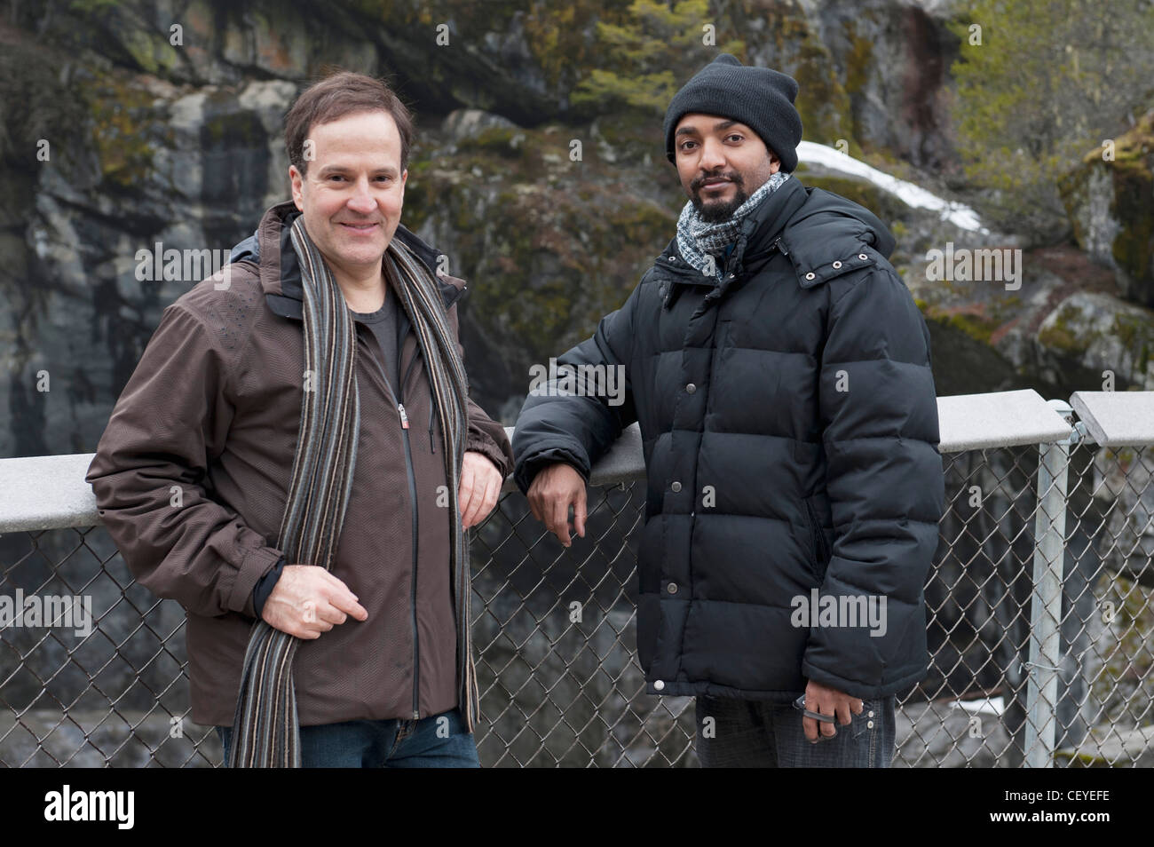 two men standing at a fenced lookout point with moss covered rock in ...
