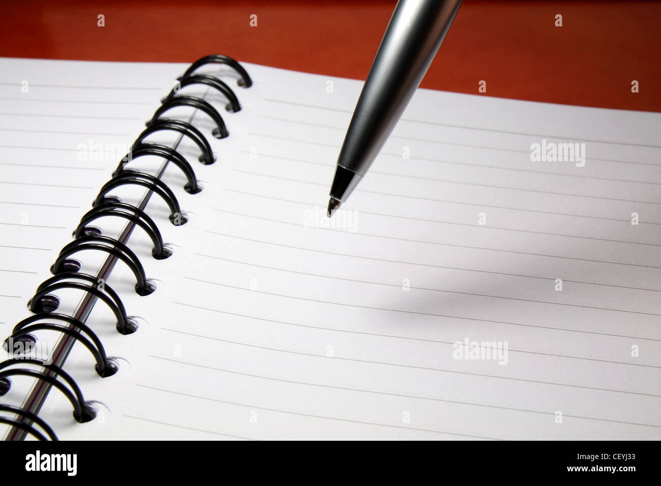 A silver ballpoint pen hovering above a blank page of a spiral notebook ...
