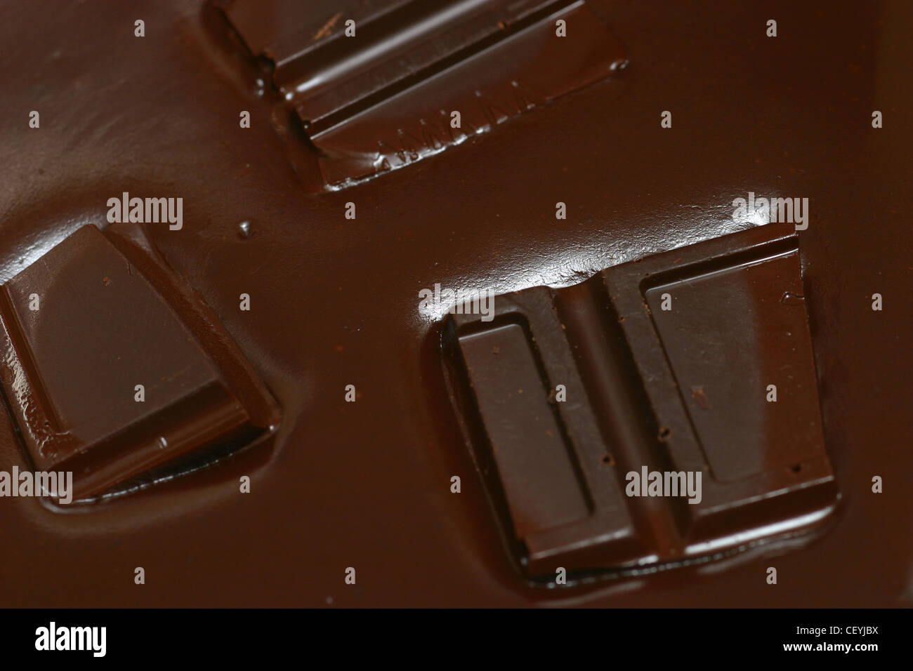 A close up of melting squares of dark chocolate, sitting in dark melted ...