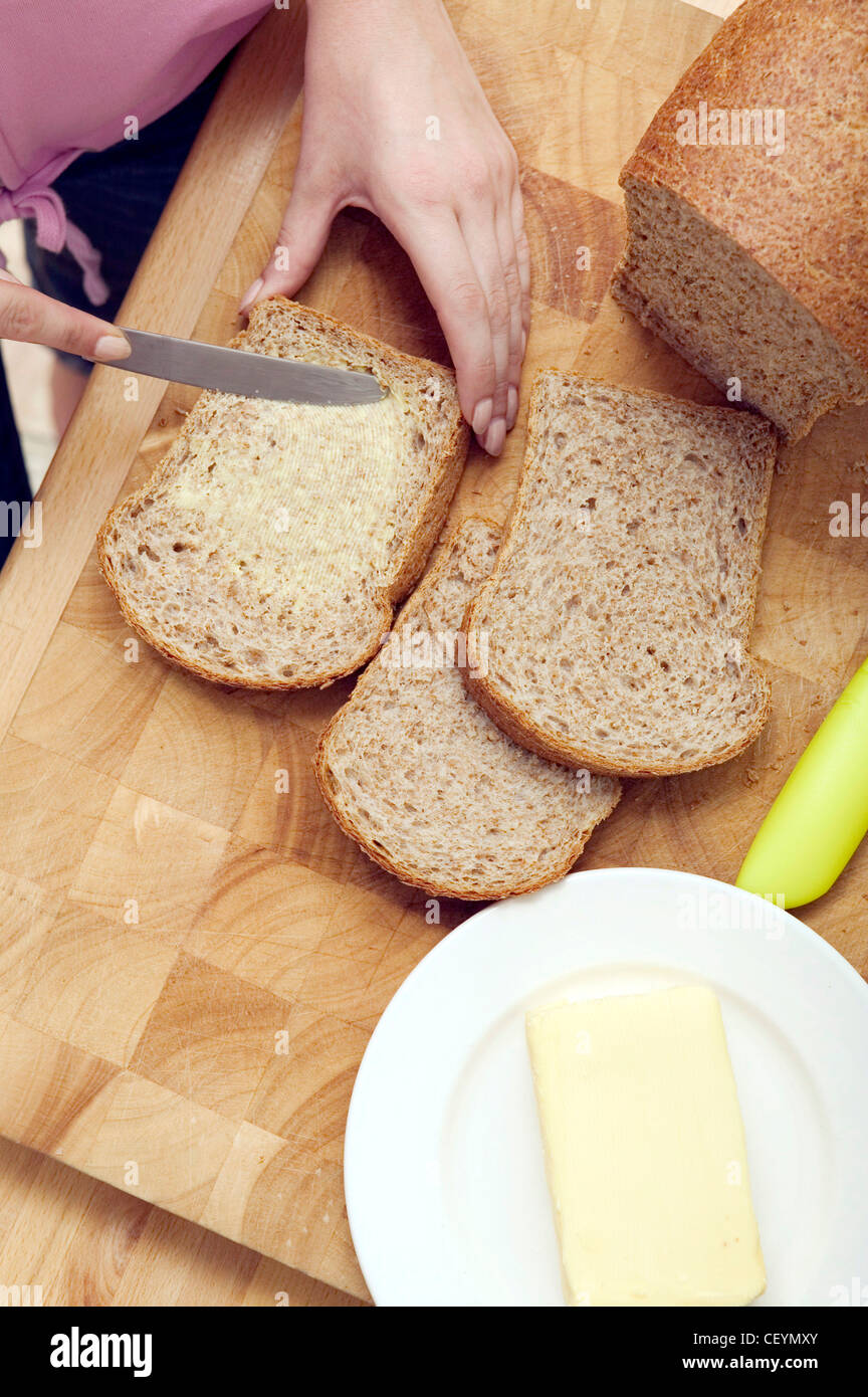 Female standing at kitchen work surface buttering slice of wholemeal ...