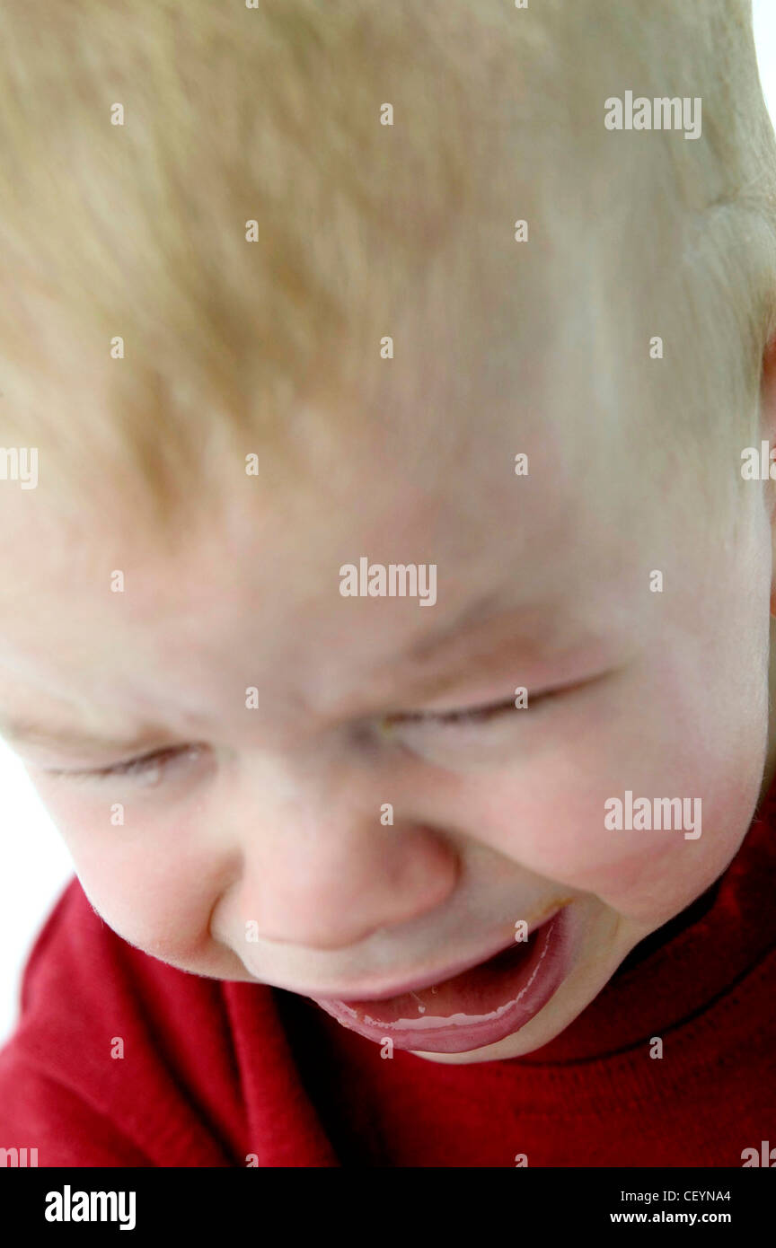 Male baby wearing red top, crying looking down against white background ...