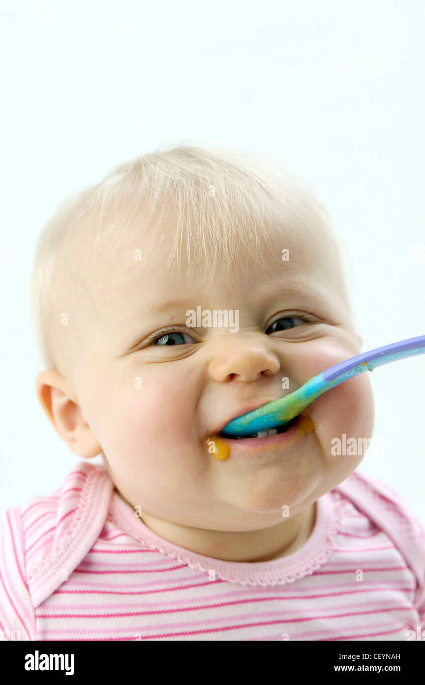 Female baby wearing pink striped babygro, being fed from plastic spoon ...