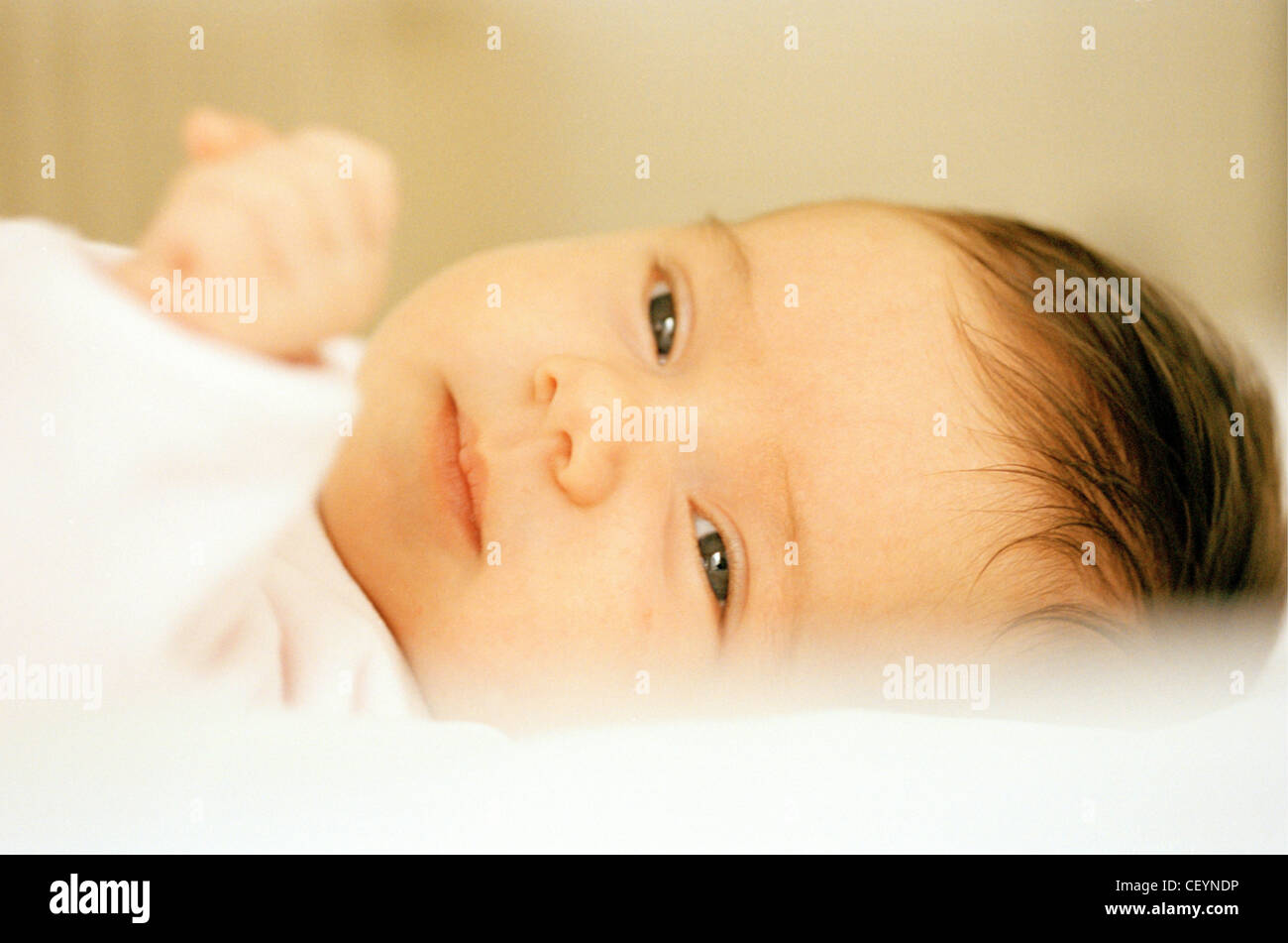 Baby with dark brown hair in pink babygro lying on back with face ...