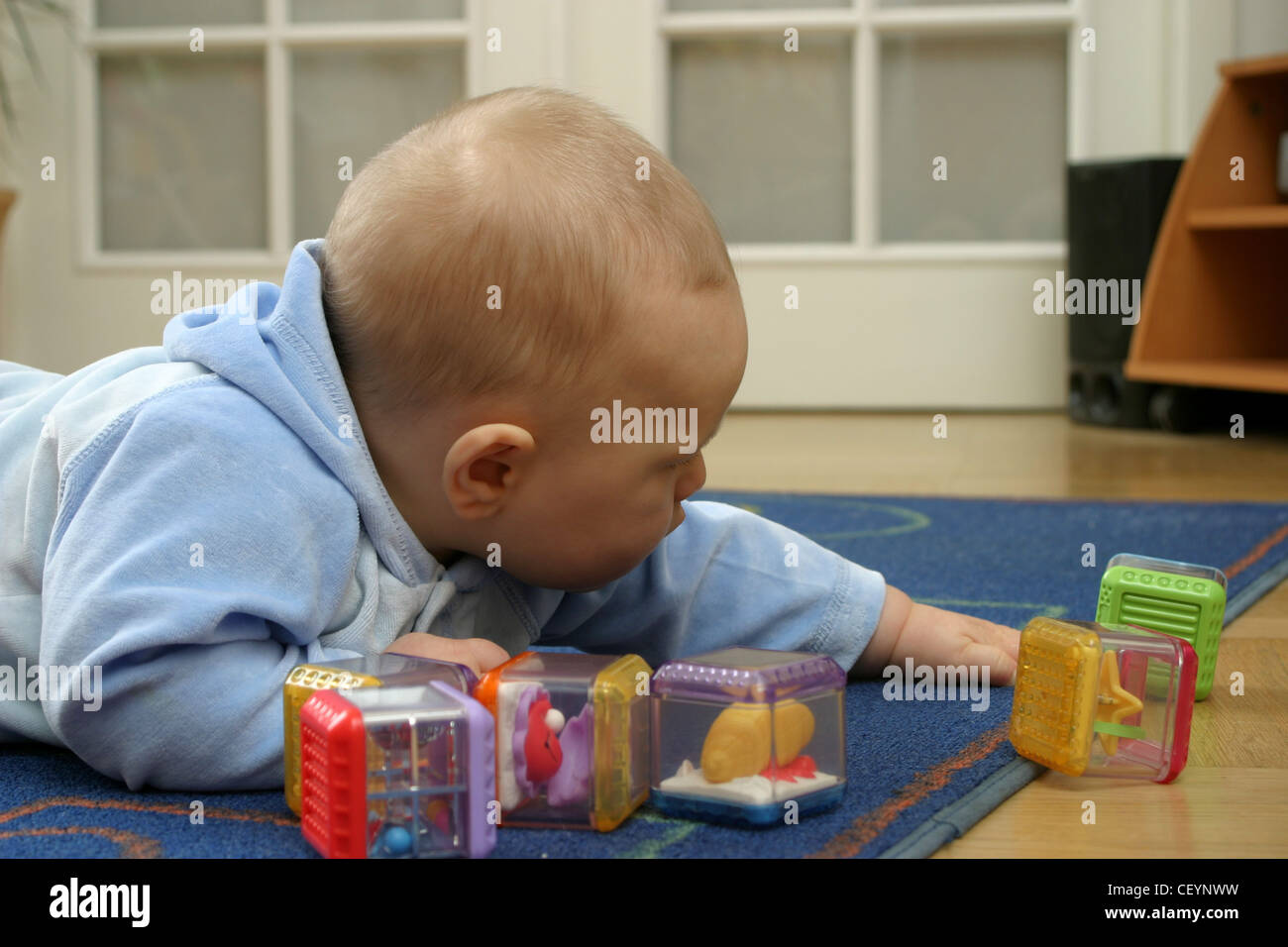 Profile of male baby lying on front on rug playing with blocks Stock ...