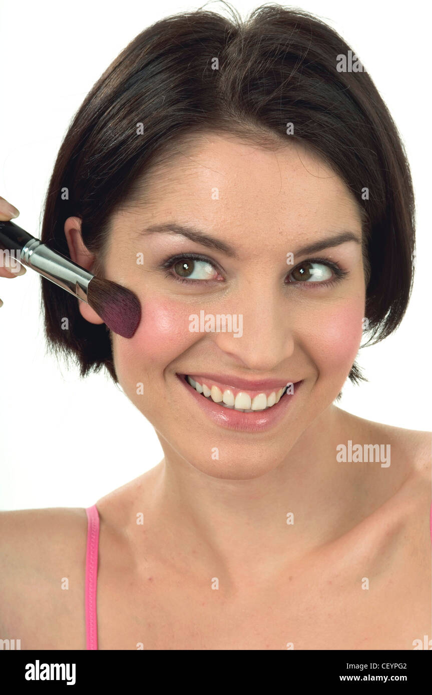 Female with straight brunette hair applying pink blusher to cheek bone ...