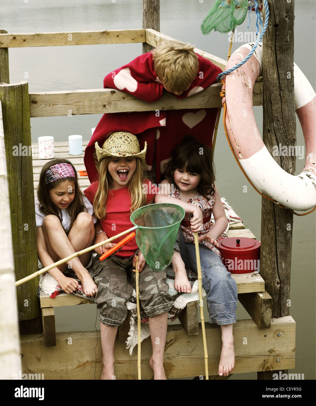 Three female children sitting on the edge of a pier legs dangling over ...