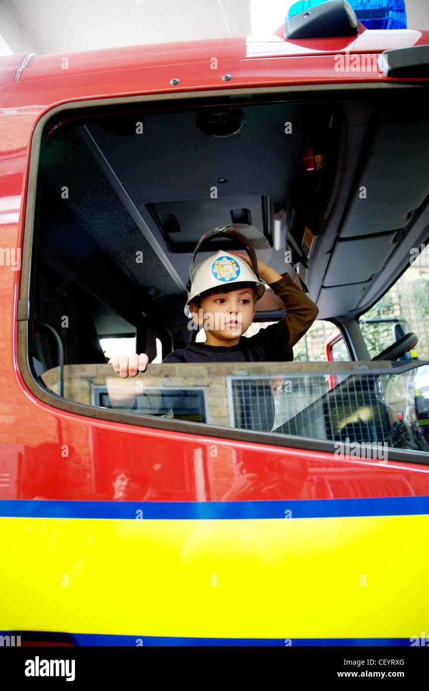 Male child sitting in fire engine wearing firemans helmet Stock Photo ...