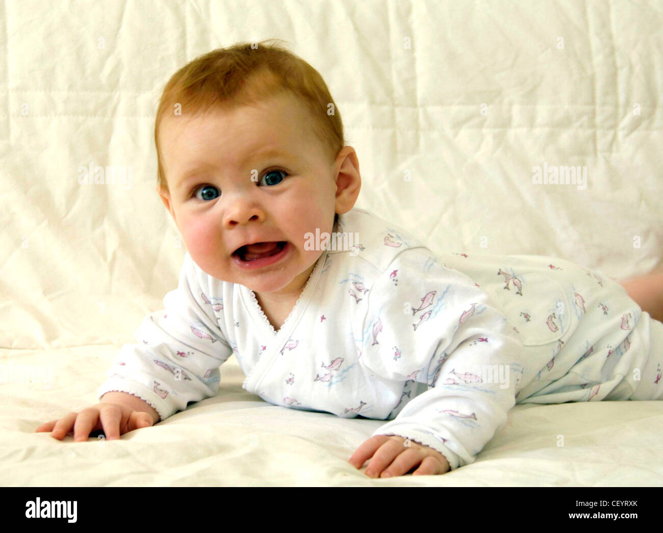 Female child wearing white baby grow lying on front on sofa leaning up ...