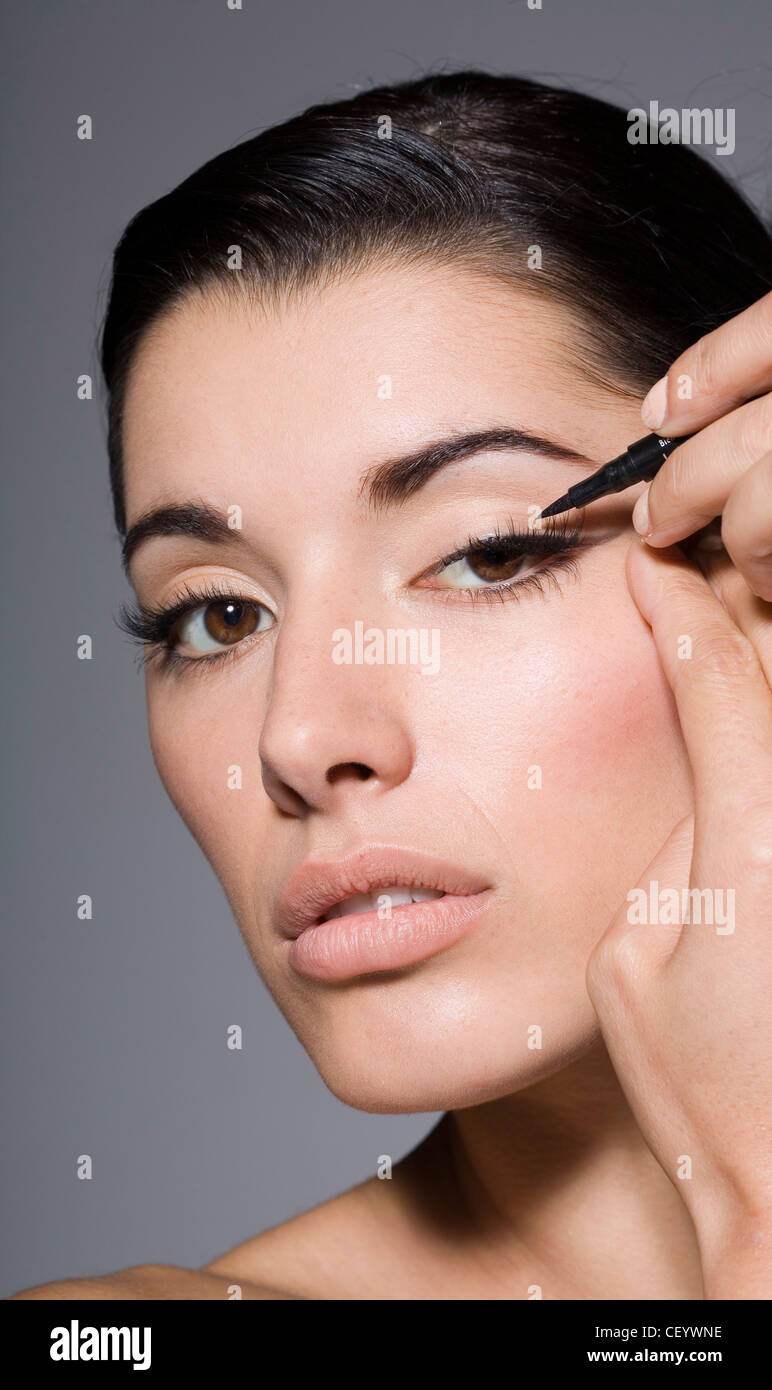 Female wearing false eyelashes applying black eyeliner with a flick ...