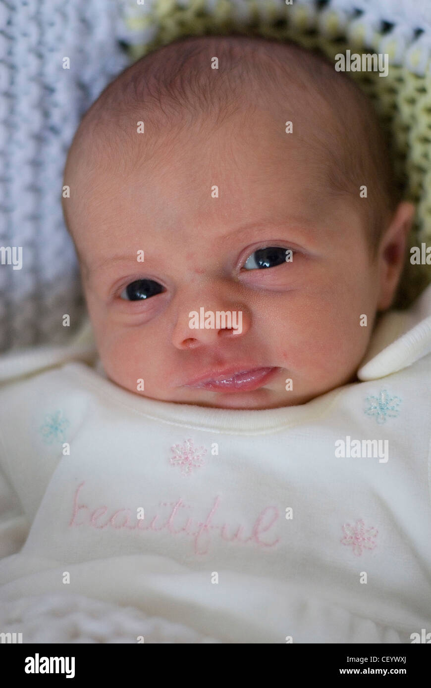 A newborn female baby dressed in a white babygrow, looking to camera ...