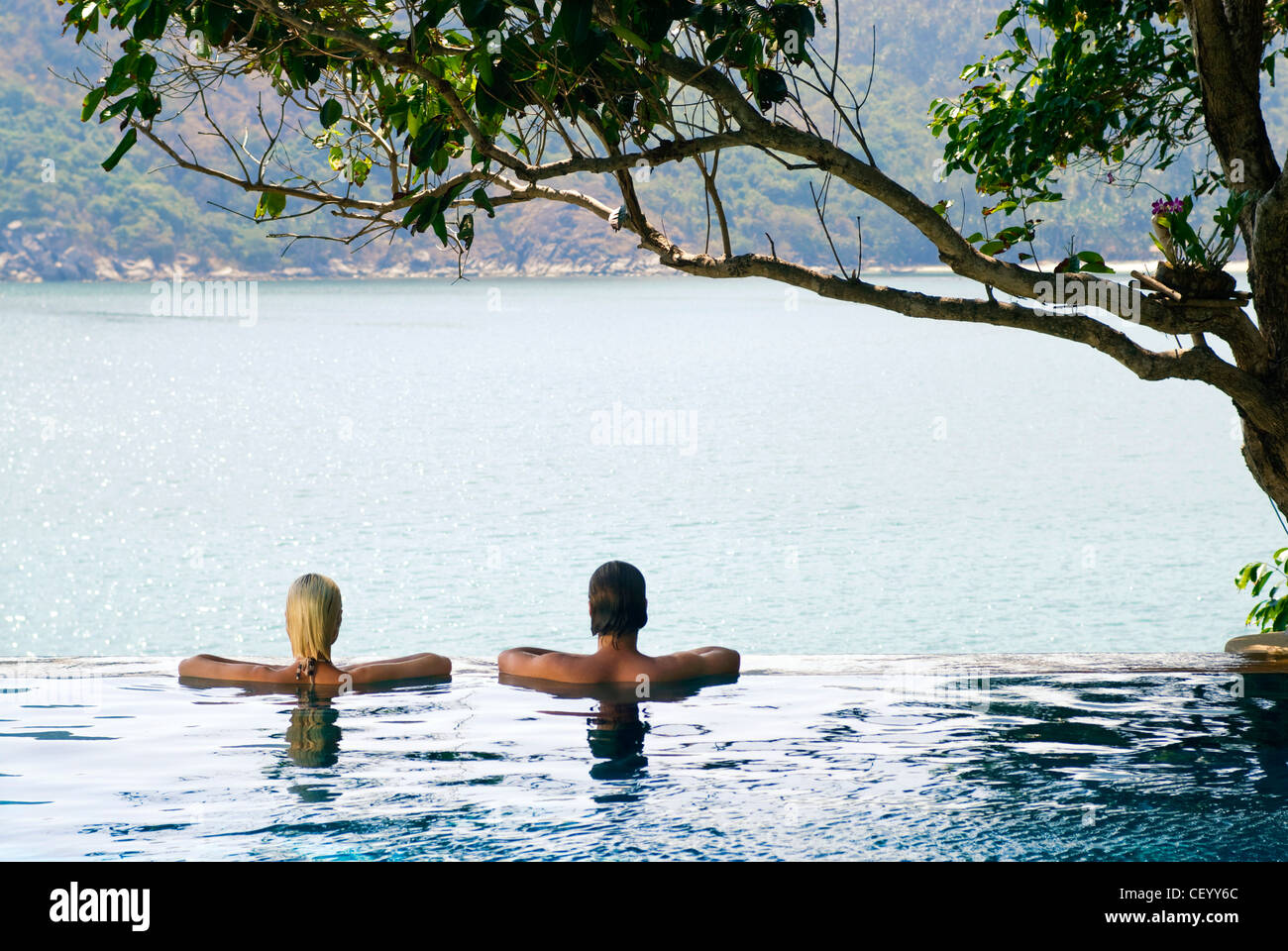 A young couple enjoys a romantic swim together at a tropical resort ...