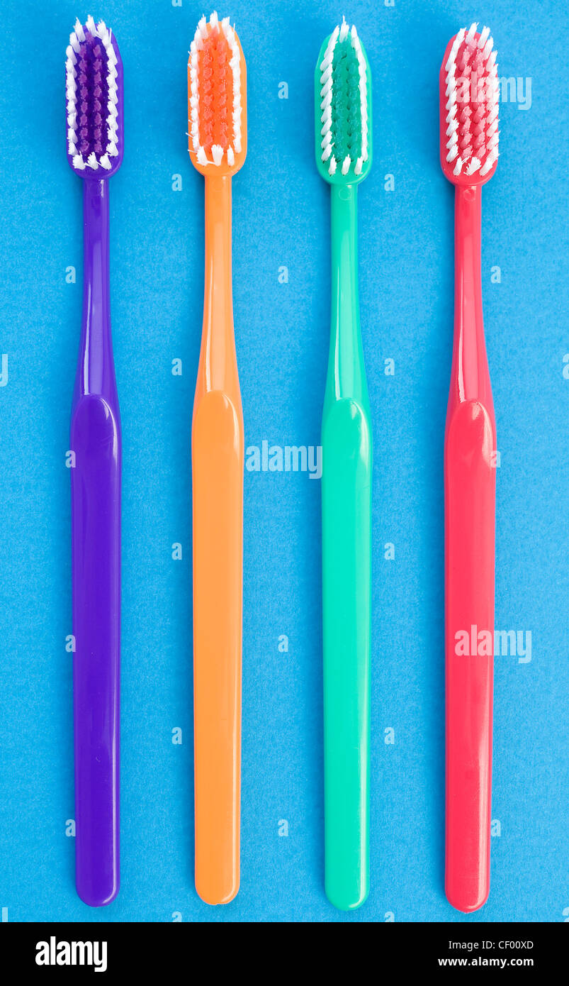 Purple, yellow, green and red toothbrushes in a row on a blue ...