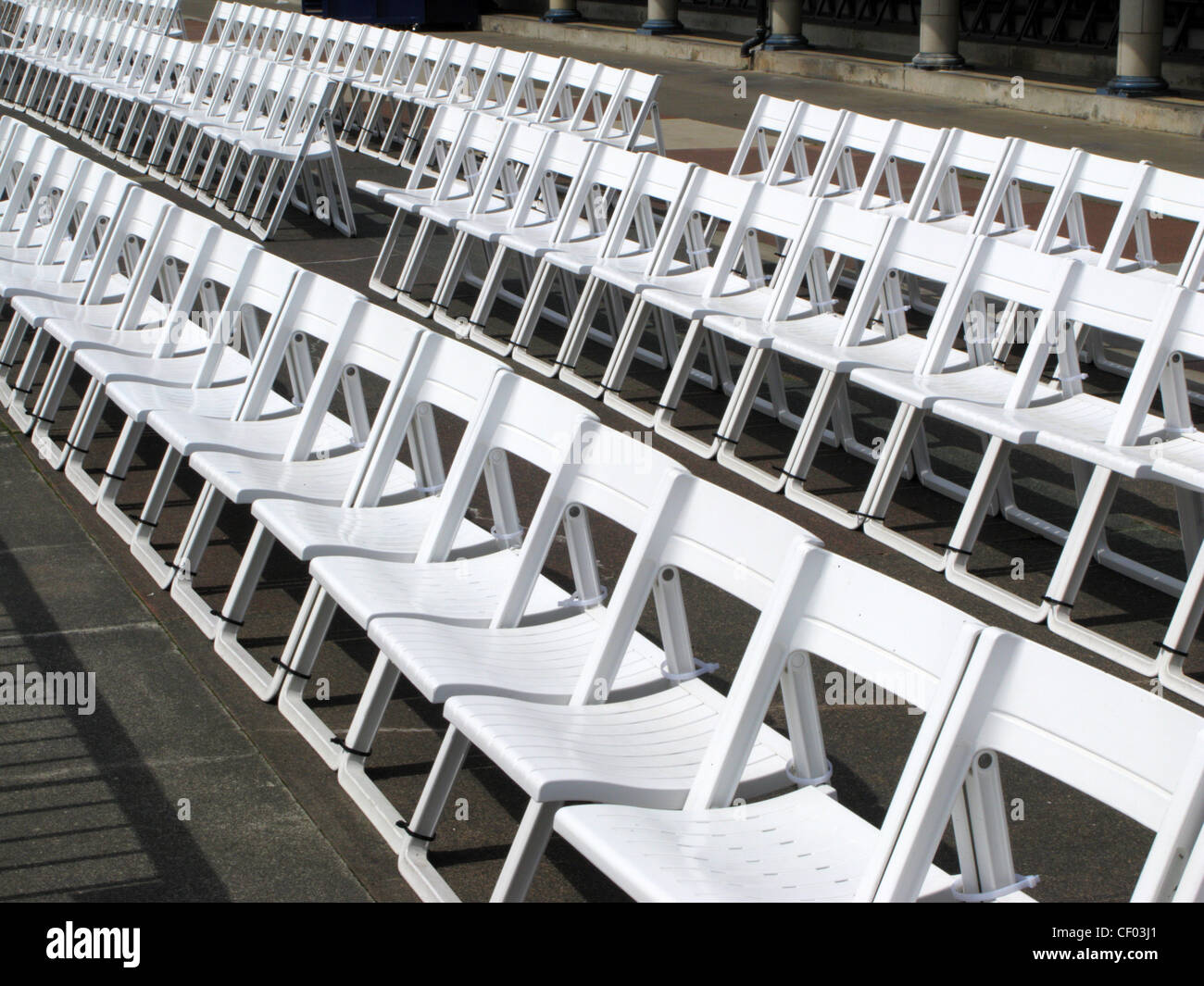 Rows of identical white seats folding chairs in the sunshine on the ...