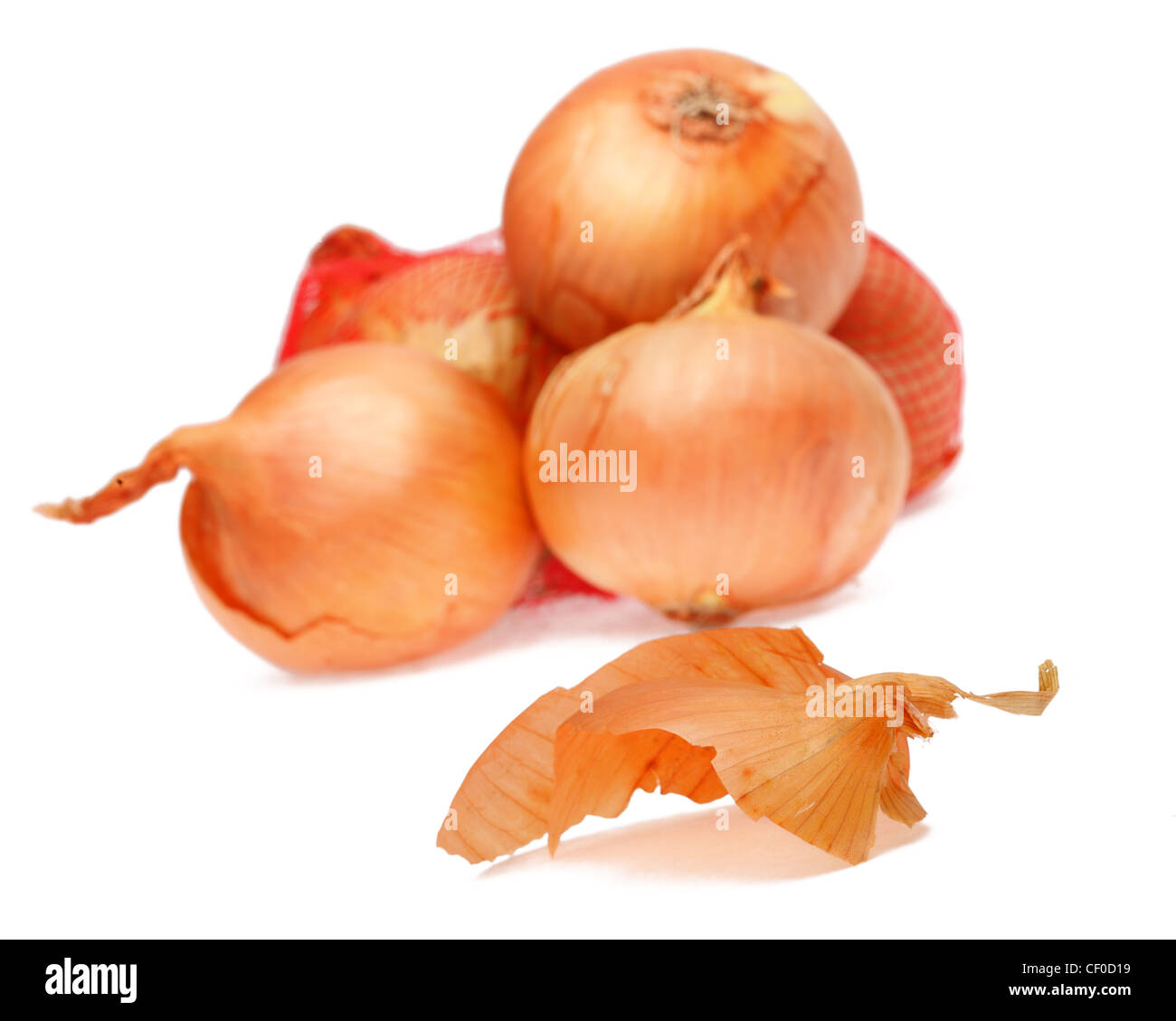 A piece of a thin onion peel in front of a heap of onions against a ...