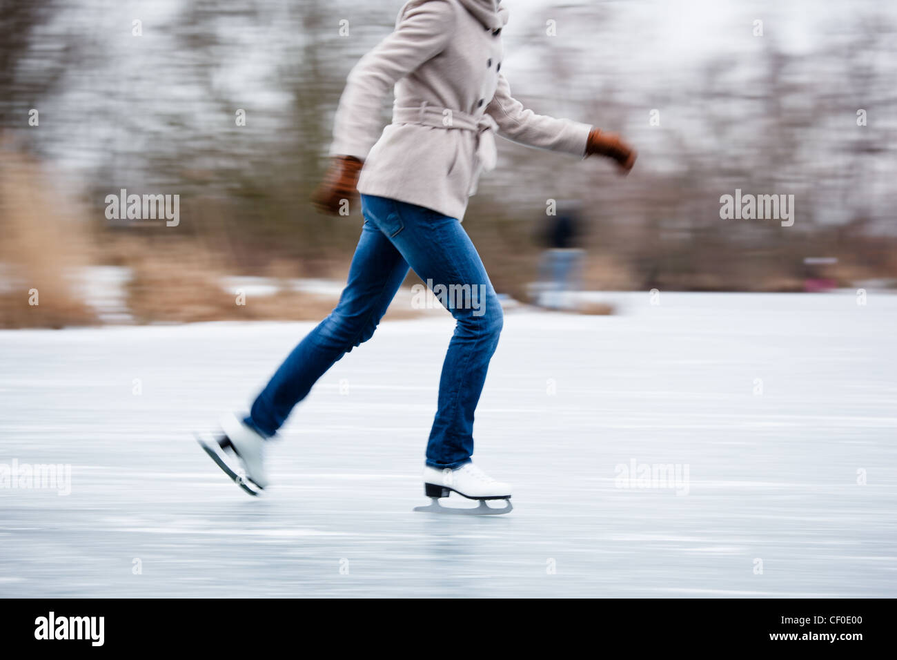 Young woman ice skating outdoors on a pond on a freezing winter day ...