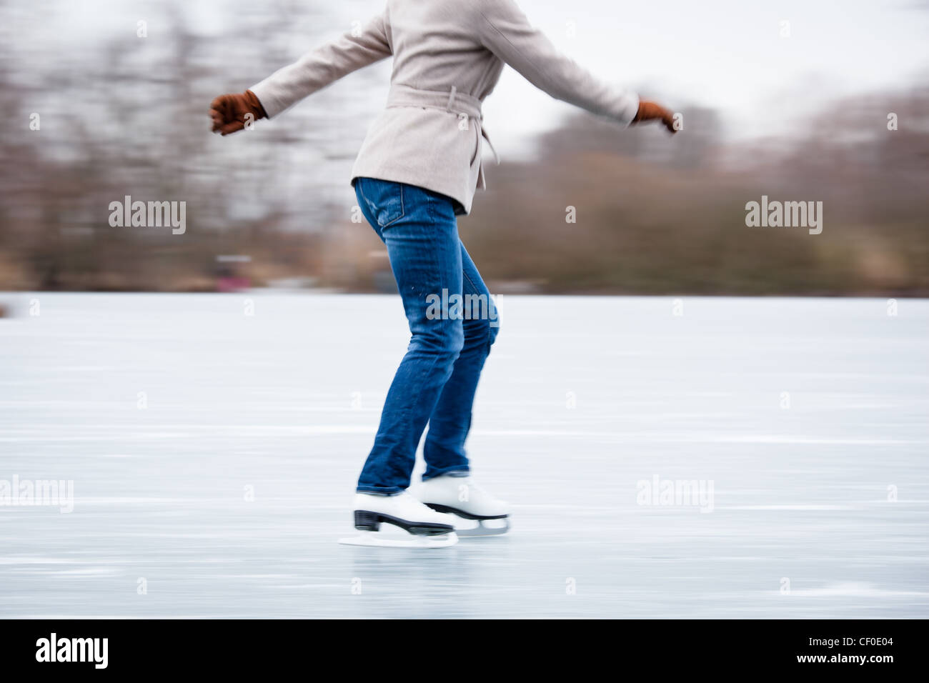 Young woman ice skating outdoors on a pond on a freezing winter day ...