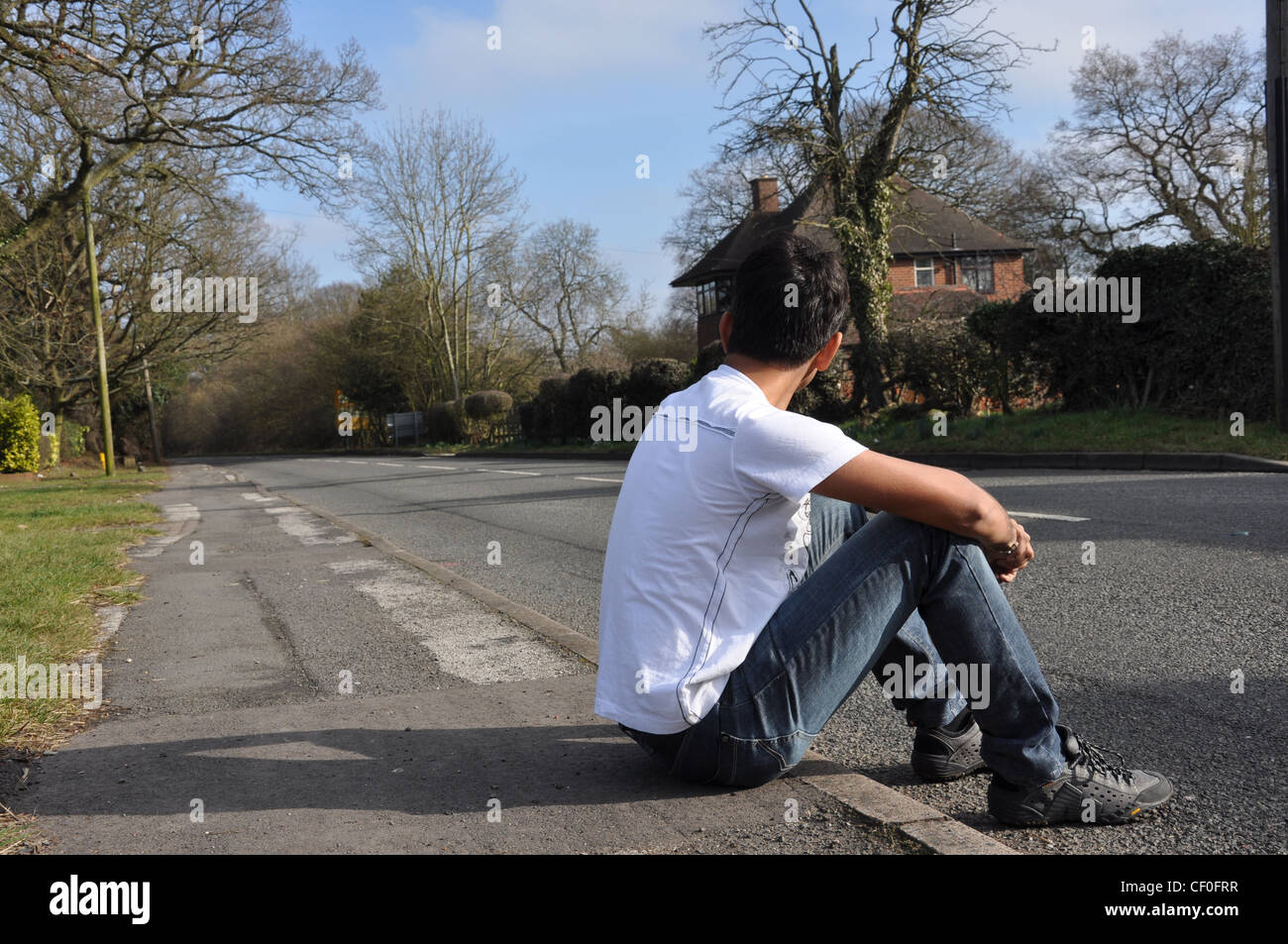 A man sitting on sidewalk, starring at an empty road Stock Photo - Alamy