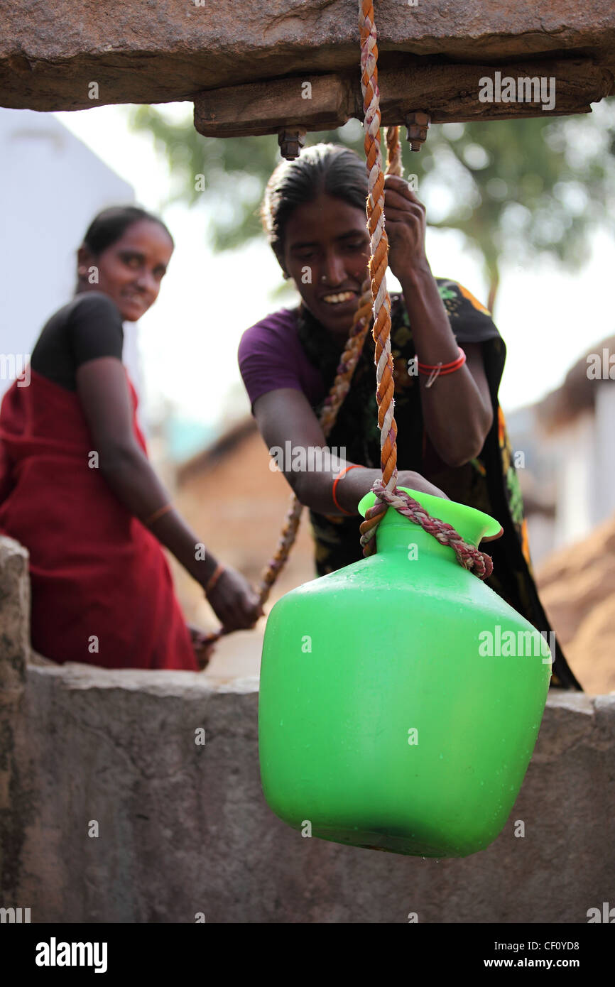 Rural women taking water from the well sharp on the green pot and rope ...