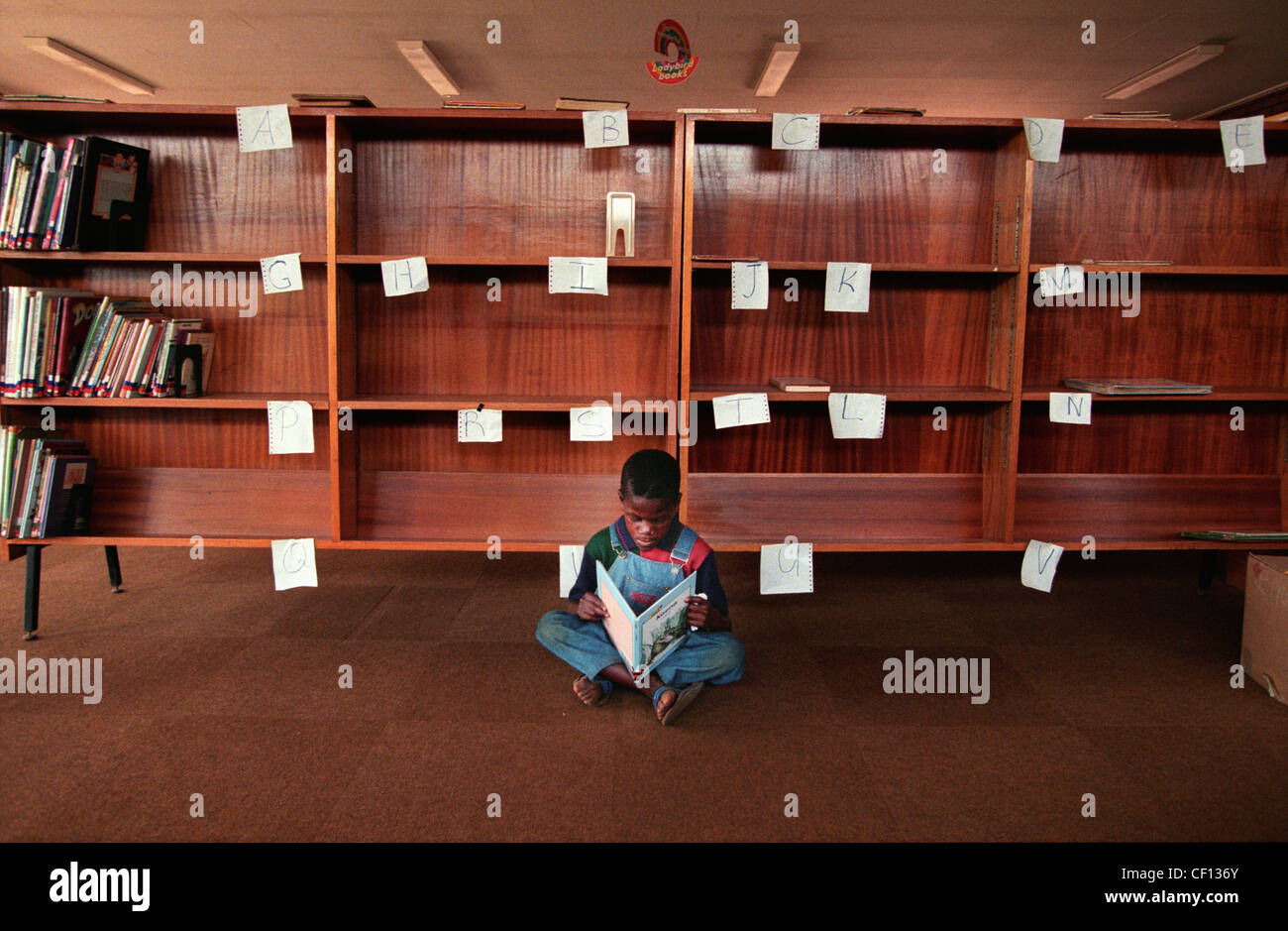 A little boy in front of the almost empty shelves of the library of his ...