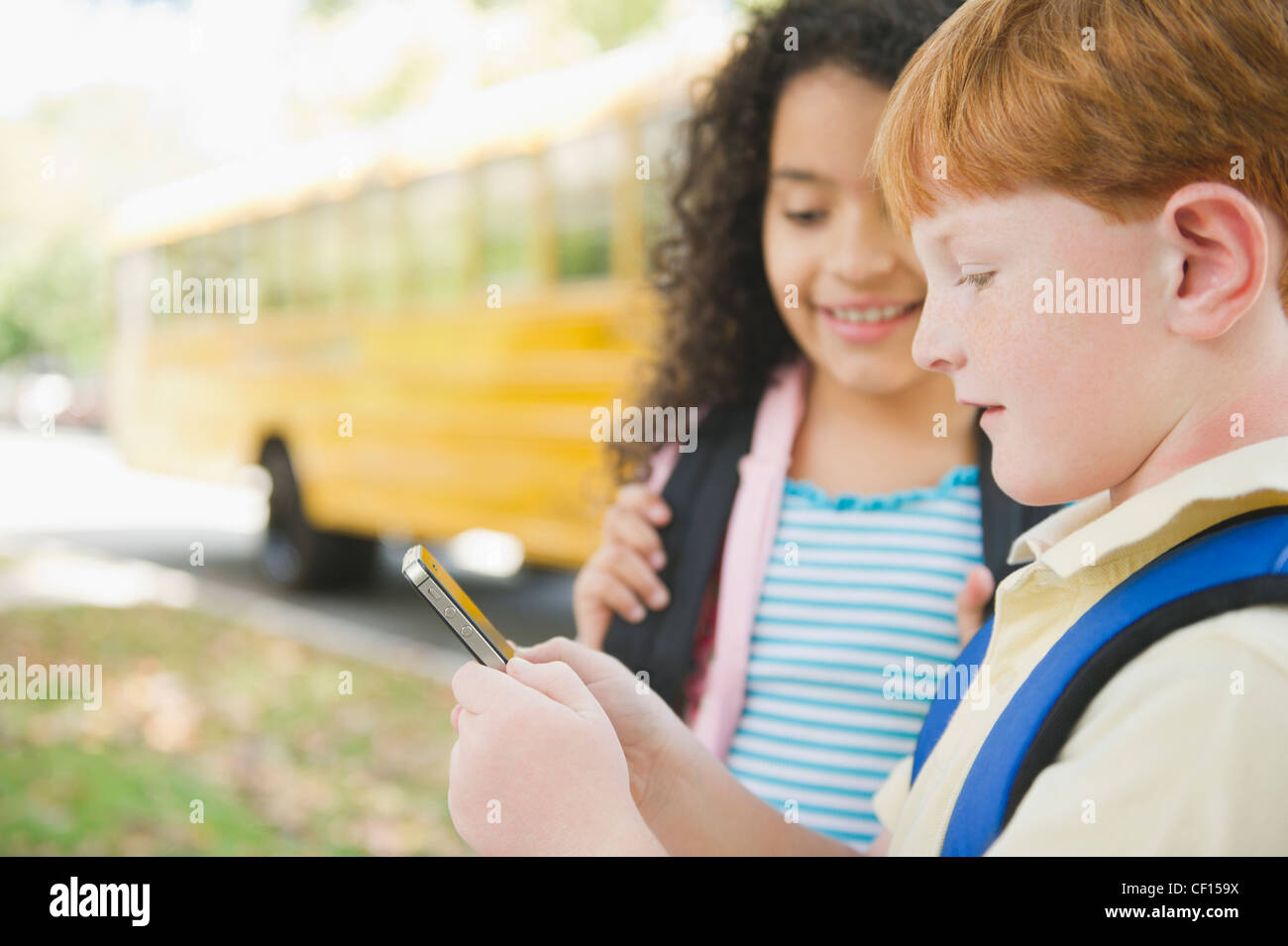 Children using cell phone while waiting for school bus Stock Photo - Alamy